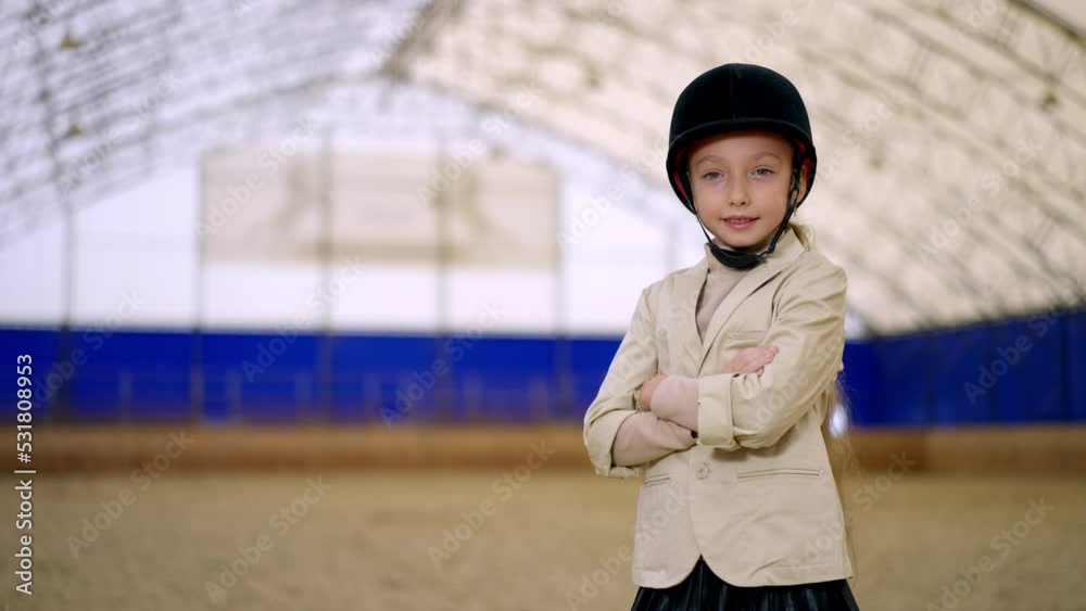 Young confident horse rider in black jockey helmet stands holding hands ...