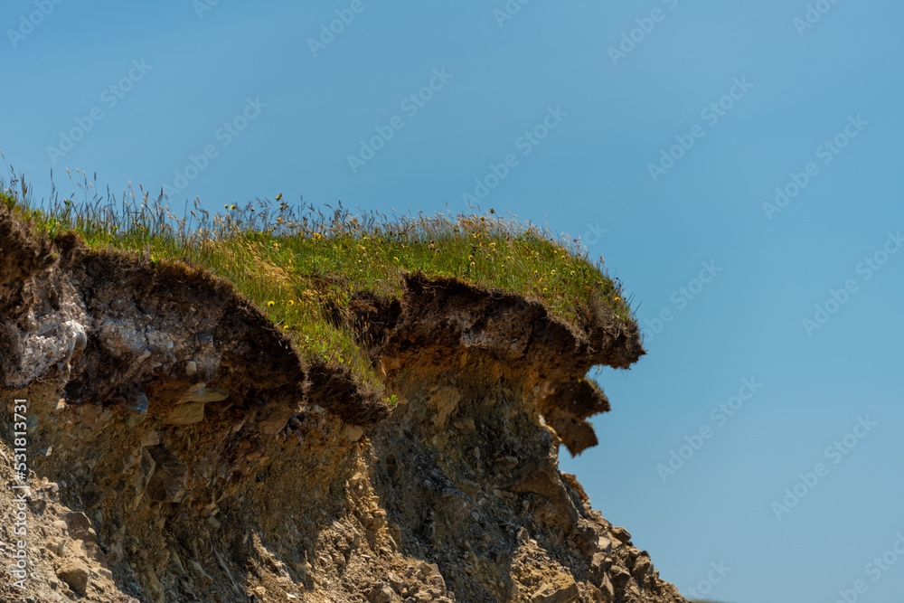 The edge of a grassy cliff with the sod hanging over the soil. The ...