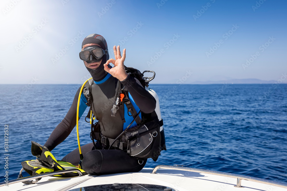 A scuba diver in full gear sits on a boat and signals the OK sign Stock ...