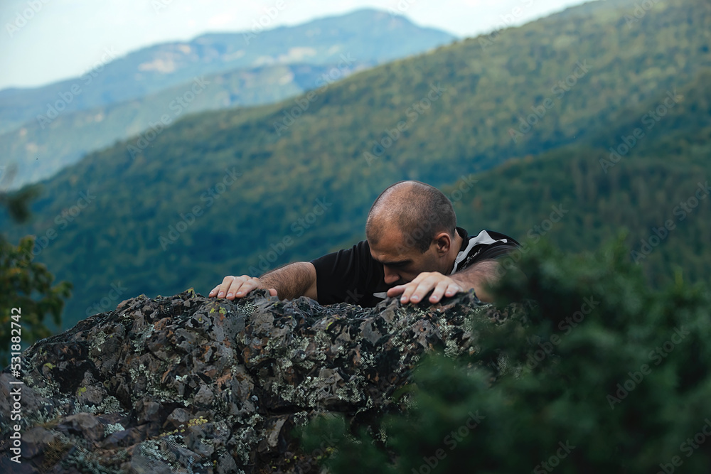 athletic manly man while climbing a high mountain, overcoming obstacles ...