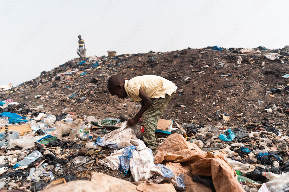 Small African boy busy recycling objects amidst heaps of plastic waste ...