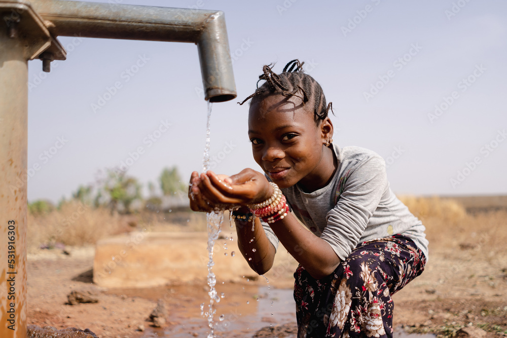 Smiling african girl tasting fresh water flowing from a tap in the ...