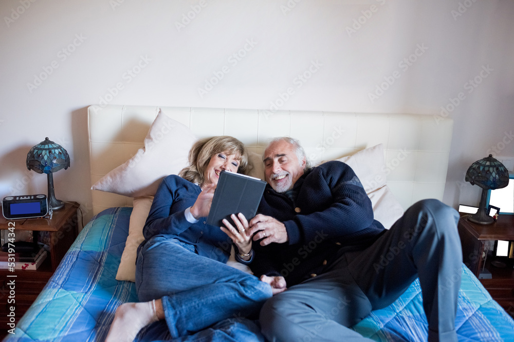 Senior married couple indoors lying in bed at home together using ...