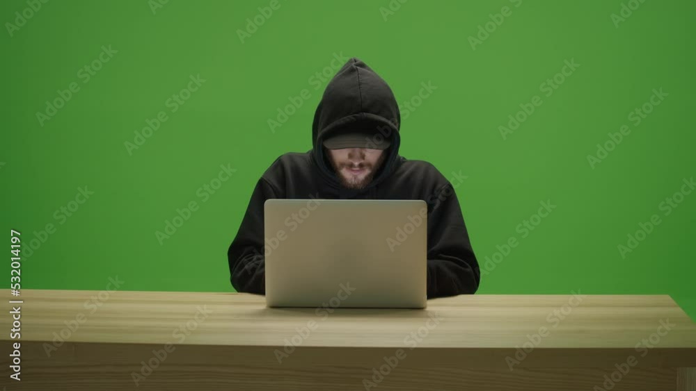 Bearded Man Hacker Wearing Sweatshirt With Hood And Cap Typing On Laptop Computer Keyboard On
