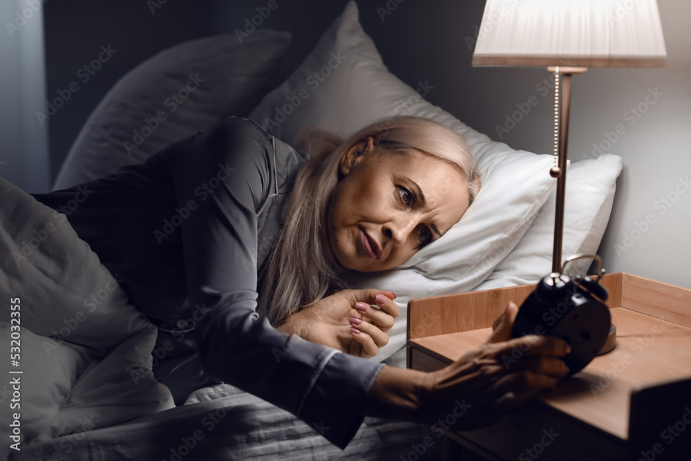 Stressed mature woman with alarm clock lying in bed at night Stock ...
