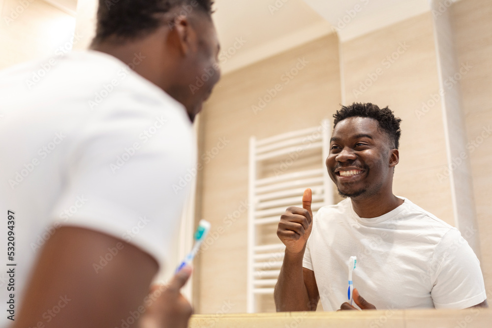Smiling African man with toothbrush cleaning teeth and looking mirror ...