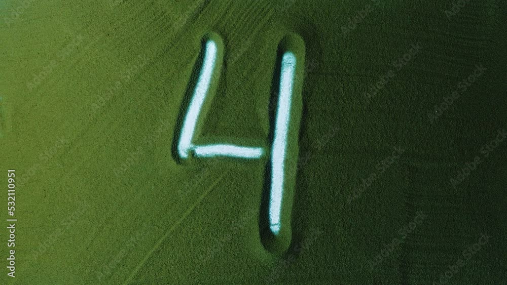 Hand drawing Number Four 4 Symbol in the Green Sand. Male hand writes a ...