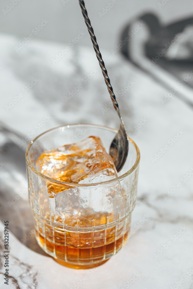 Picture of mixing a cube of ice with a bar spoon to a whiskey cocktail ...