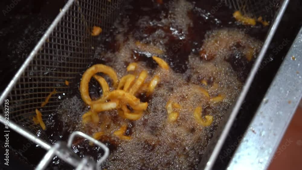 Golden crunchy and crispy curly fries in sieve basket cooking in ...