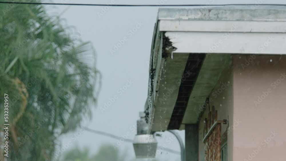 A house in the rain as water droplets form and fall off of the corner ...