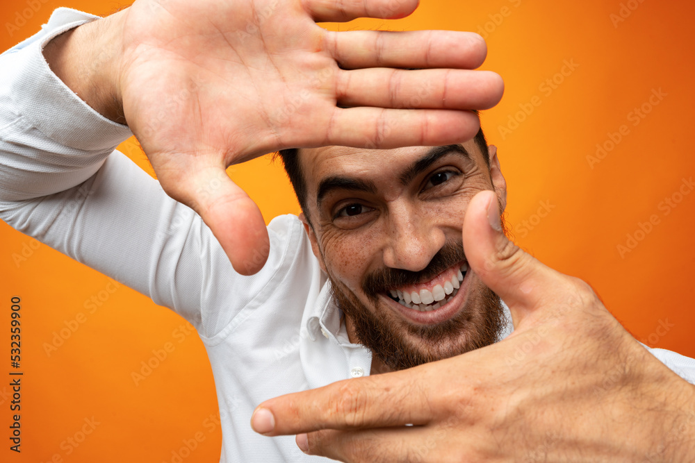 Smiling young man looking at camera and making frame gesture on orange ...