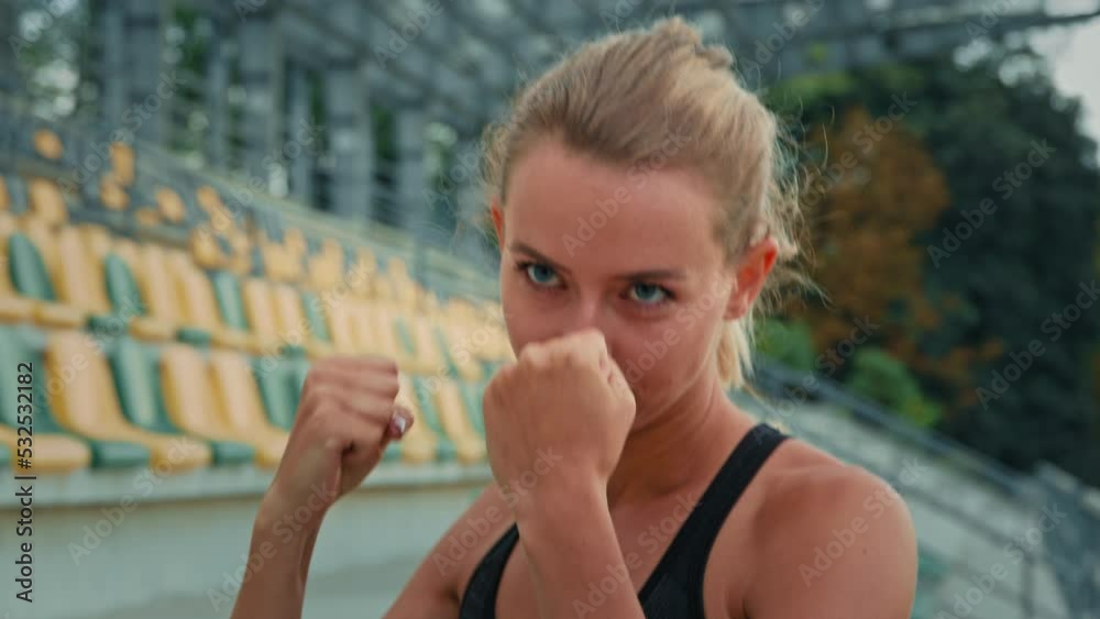 Motivated female fighter athlete with clenched fists standing in boxing ...