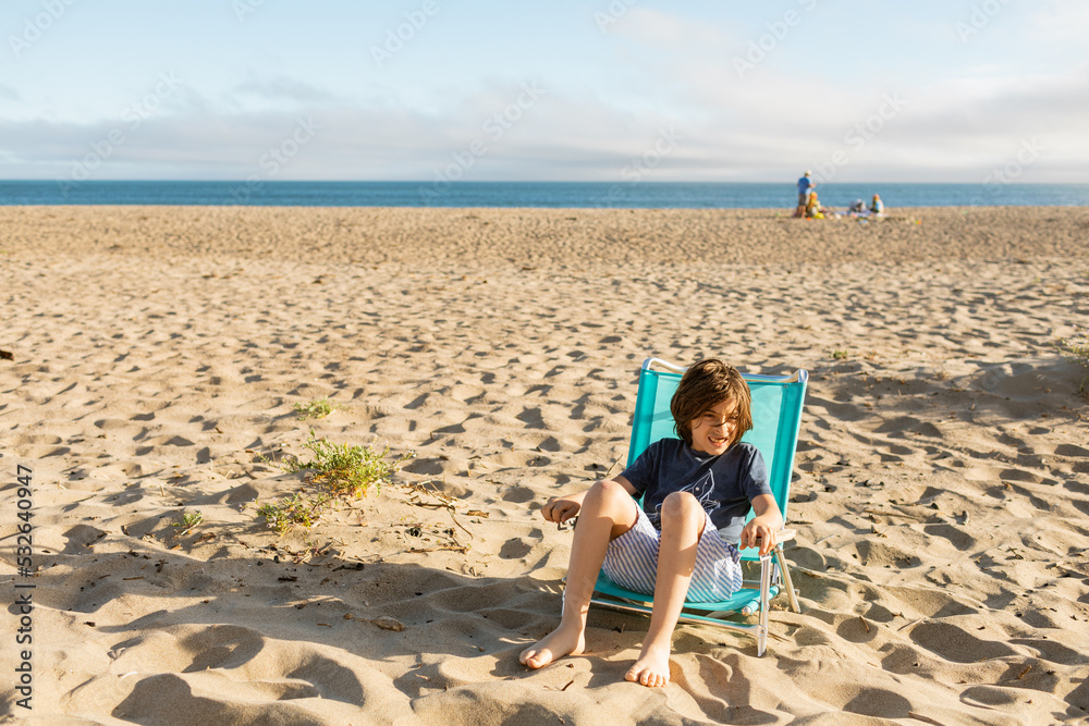 Boy sitting on folding chair at the beach Stock Photo | Adobe Stock