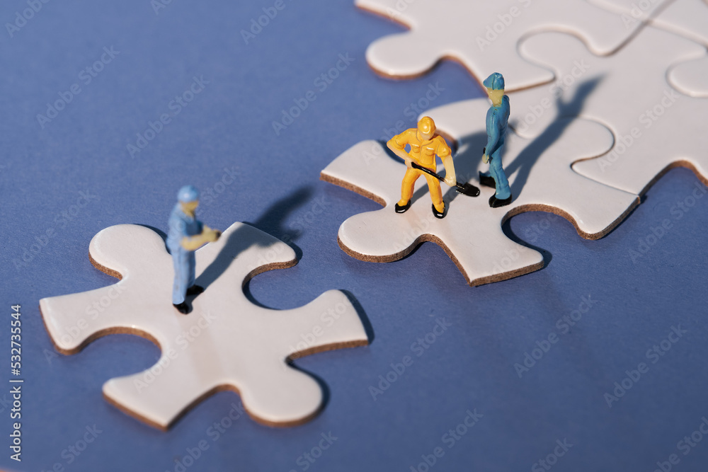 Team of tiny worker miniature figures on linked jigsaw puzzle pieces ...
