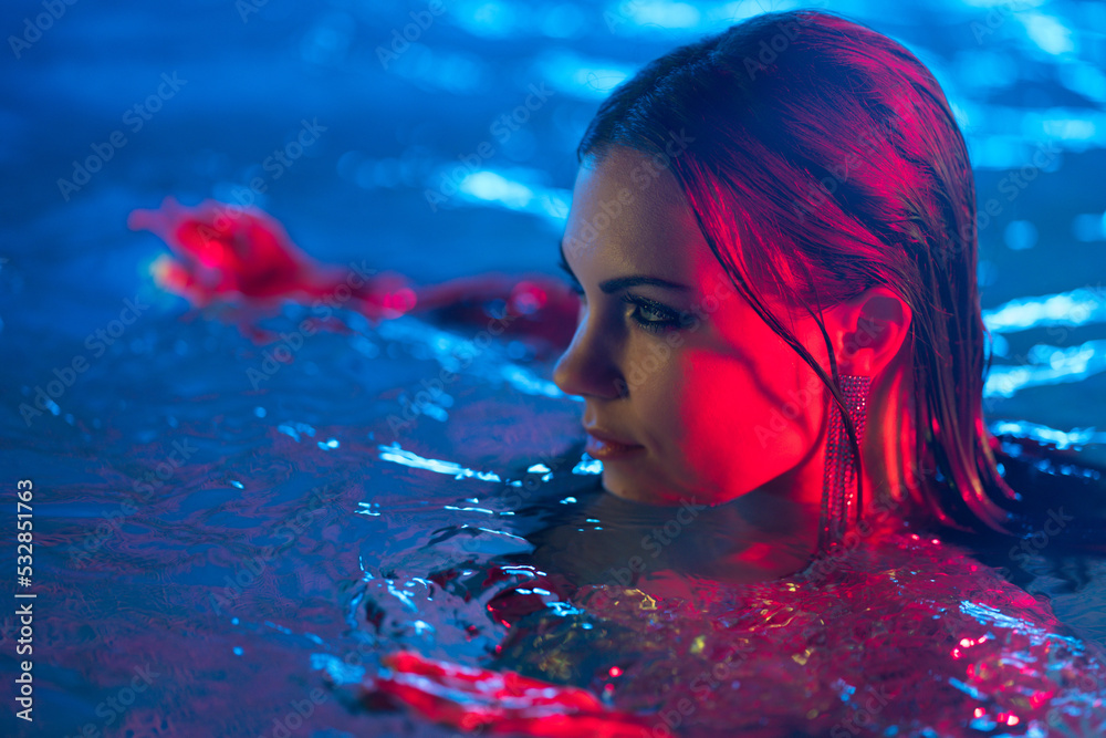 Sexy dangerous woman in swimming pool water under neon colorful light ...