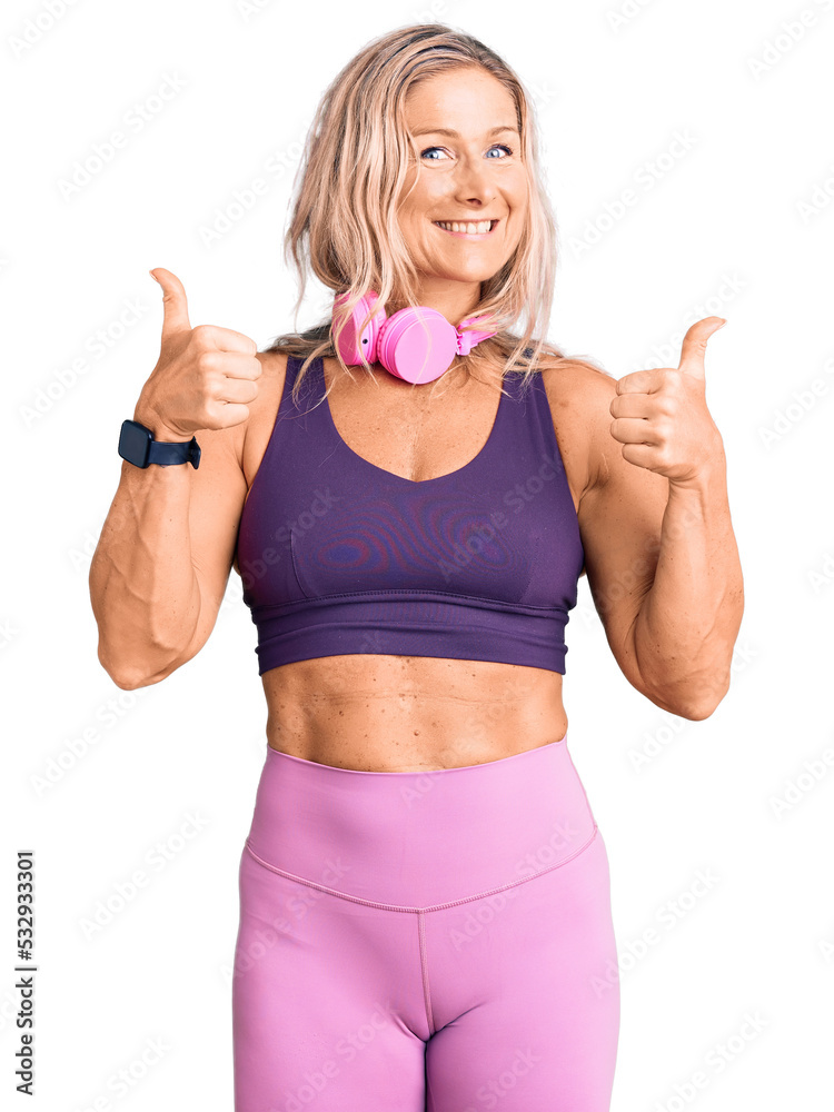Middle age fit blonde woman wearing gym clothes and using headphones ...