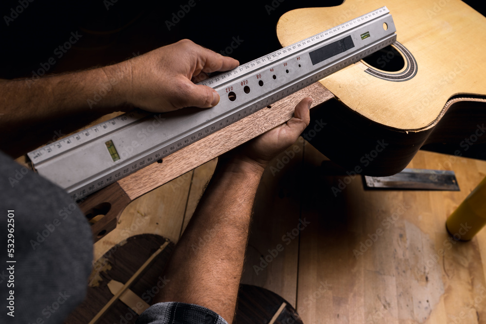 Luthier measuring neck of a guitar with a precision ruler. Dark ...