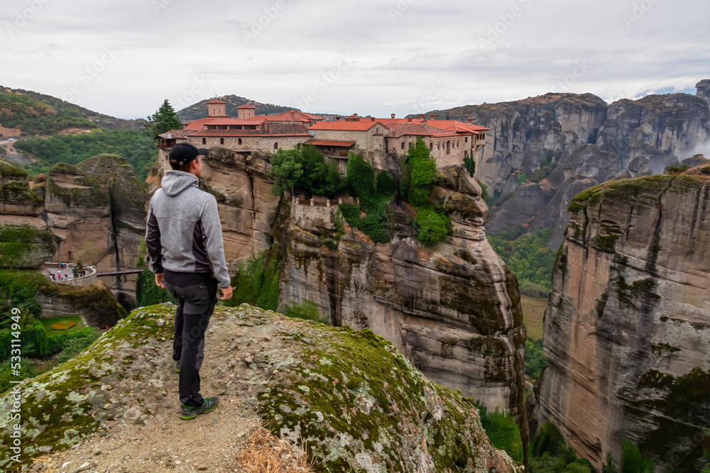 Man standing on cliff edge with panoramic view of Holy Monastery of ...