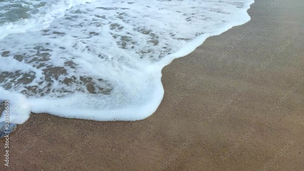 Sea waves with white foam roll on the sandy beach of the seashore close ...