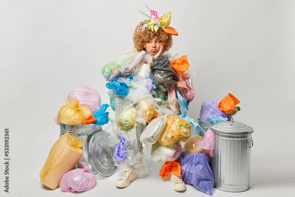 Sad eco friendly woman looks sadly away poses around garbage bins with ...
