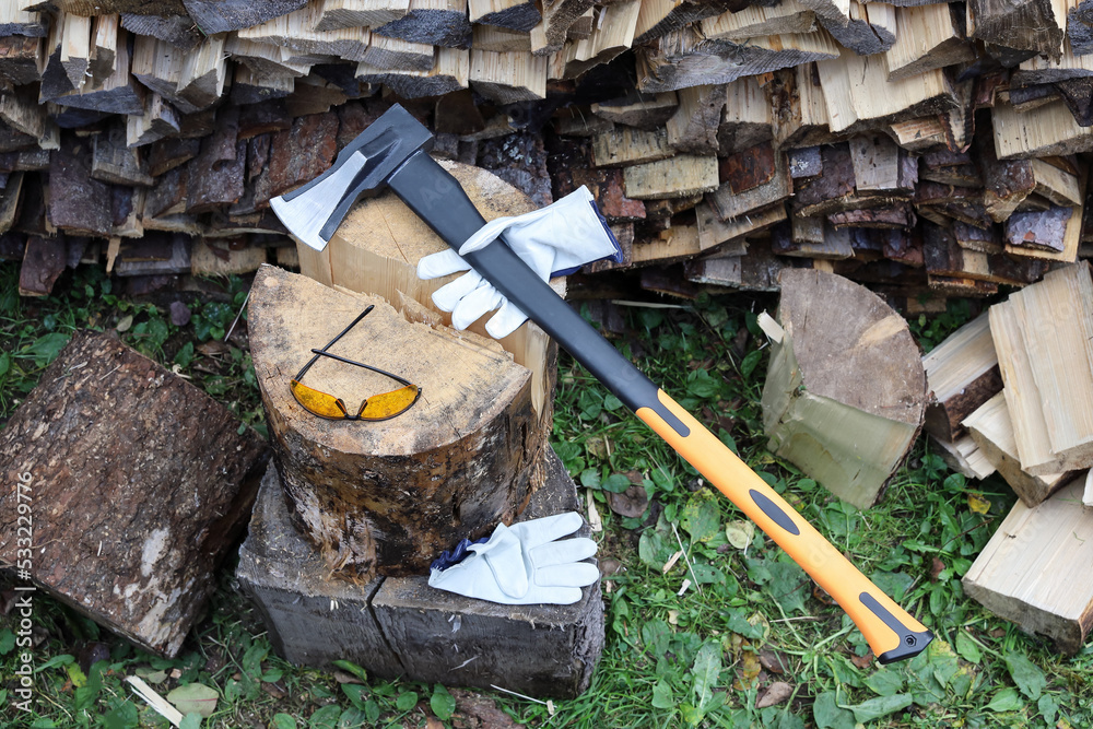 Axe for splitting in crack of wooden end and protective glasses and gloves on stump, harvesting ...