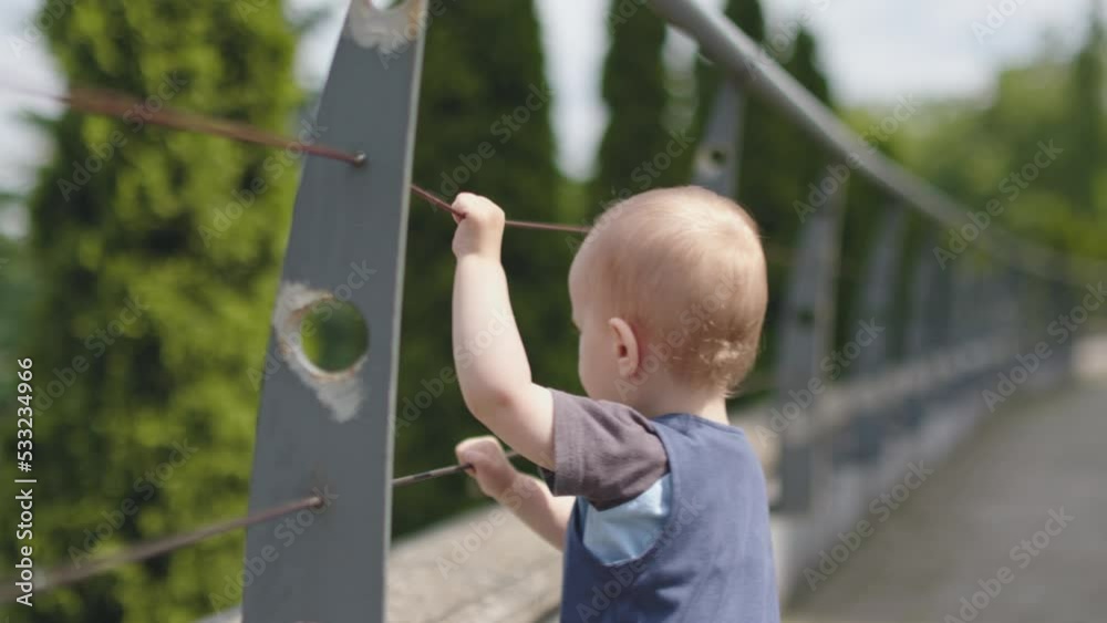 lonely baby child holding metal barrier string of fence looking behind ...