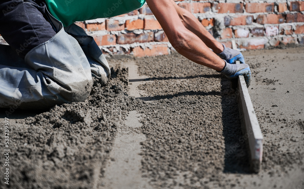 Close up of man builder placing screed rail on the floor covered with ...