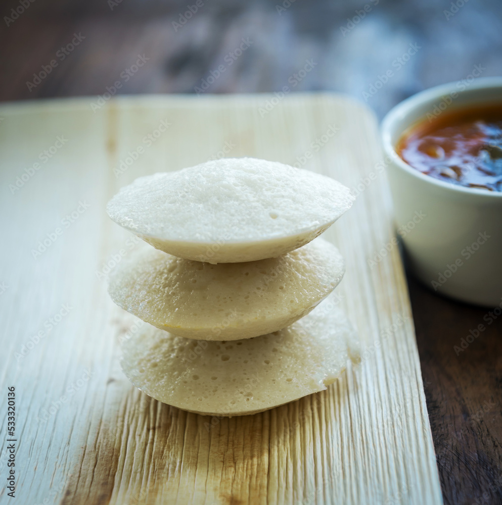 Rice idlis stacked on each other with bowl of sambar at the background ...
