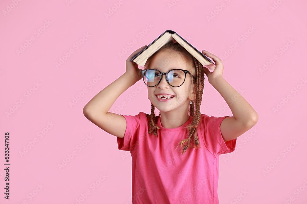 Back to school concept. Smiling pretty little school girl in glasses is holding book over head ...