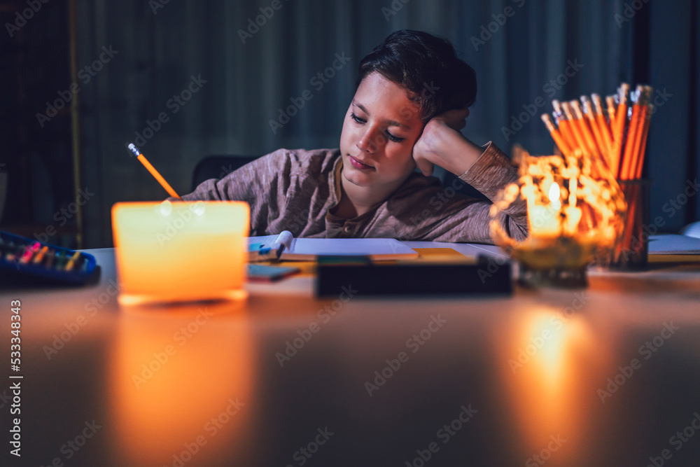 Little boy studying in low light with a burning candle. Power outage ...