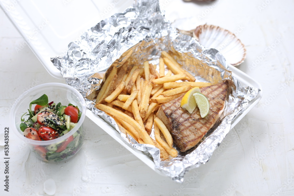 Tuna steak served with fries and salad mix in takeaway boxes. Fish and ...