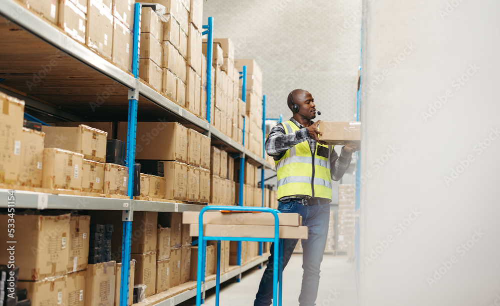 Warehouse picker pulling a flat box from a shelf with a headset on ...