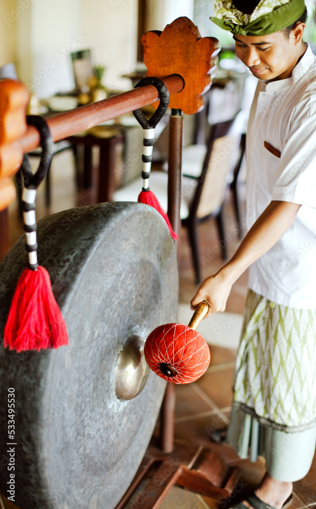Young Balinese waiter hits gong to welcome guests to a resort ...