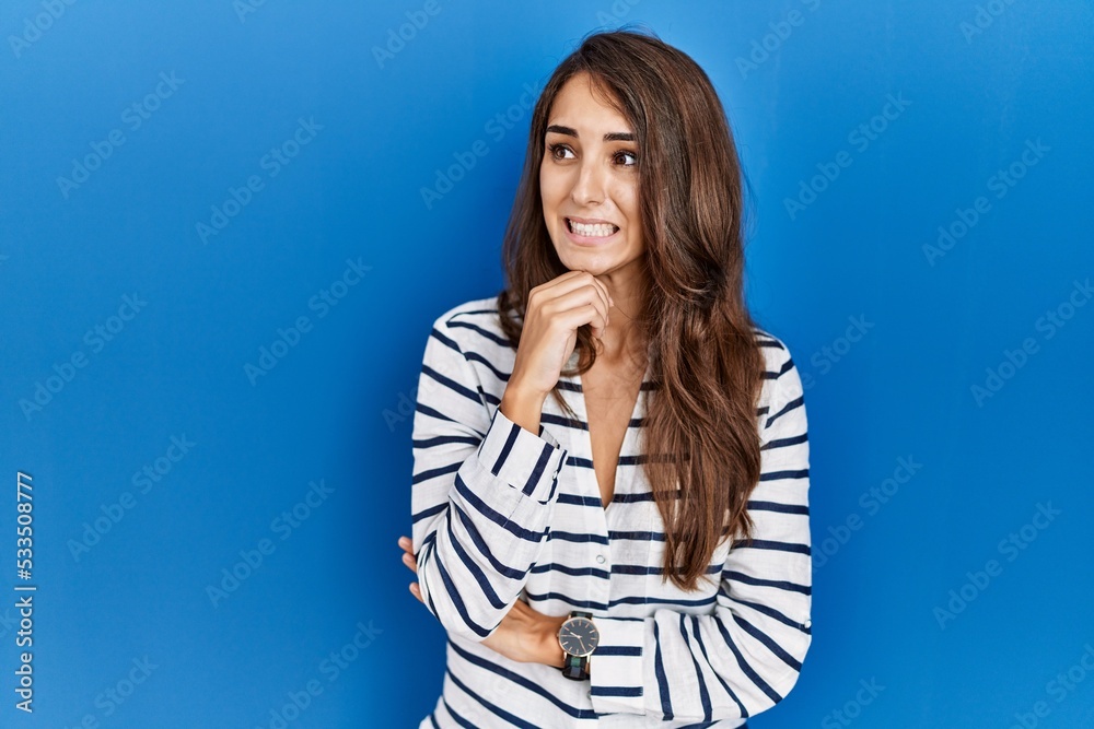 Young hispanic woman standing over blue isolated background thinking ...