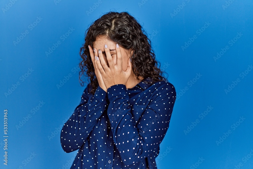 Young brunette woman with curly hair wearing casual clothes over blue ...