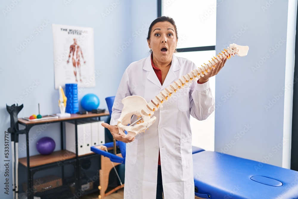 Middle age hispanic woman holding anatomical model of spinal column ...