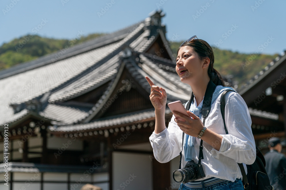 cheerful asian girl tourist finger pointing at a landmark in distance ...