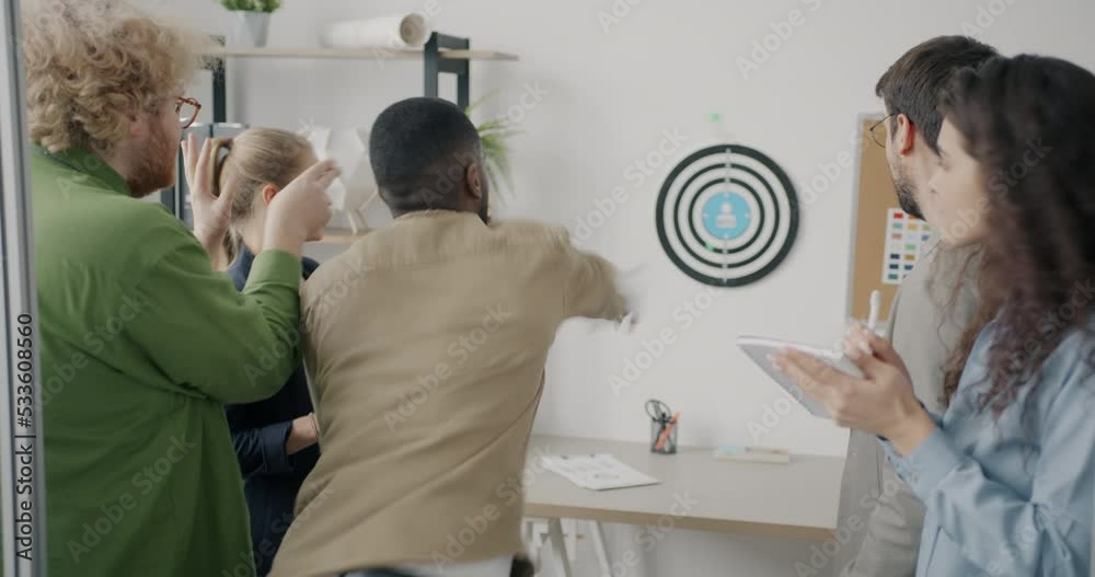 African American man is playing darts at work while colleagues diverse ...