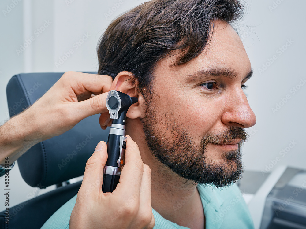 Adult man during ear exam at hearing clinic. Audiologist examining male ...