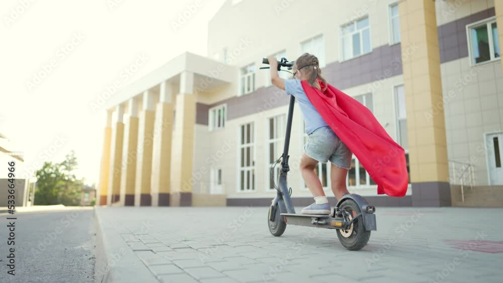 Kid in superhero costume is riding an electric scooter on road.Child ...