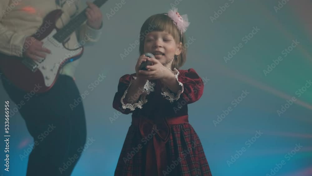 Little girl on stage in vintage dress, she sings into microphone and ...