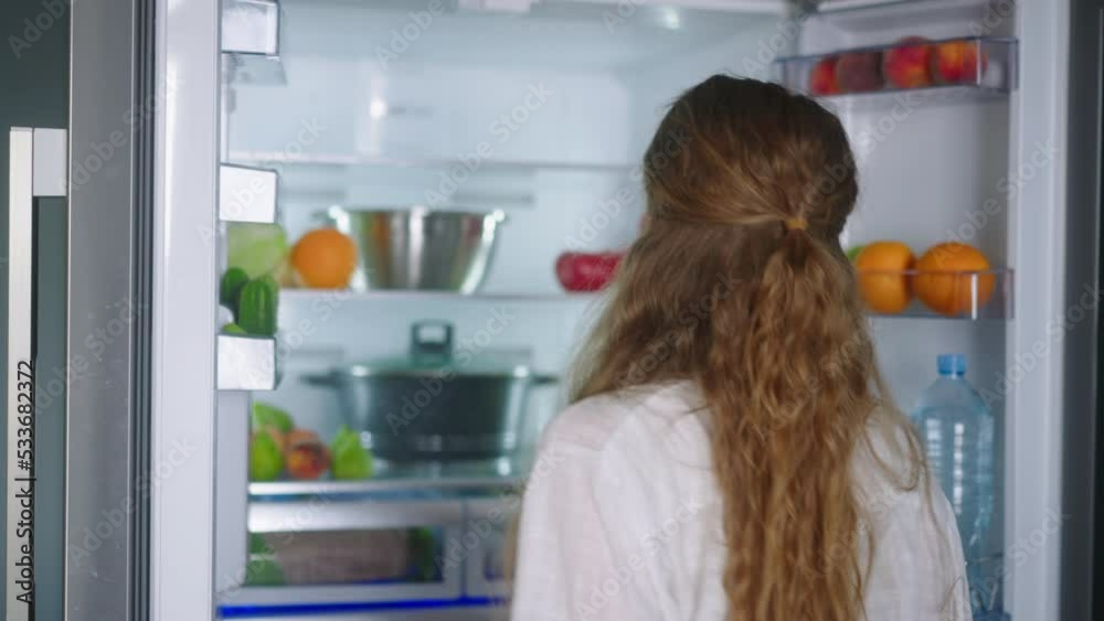Young woman taking vegetables from fridge. Girl getting a tomato from ...