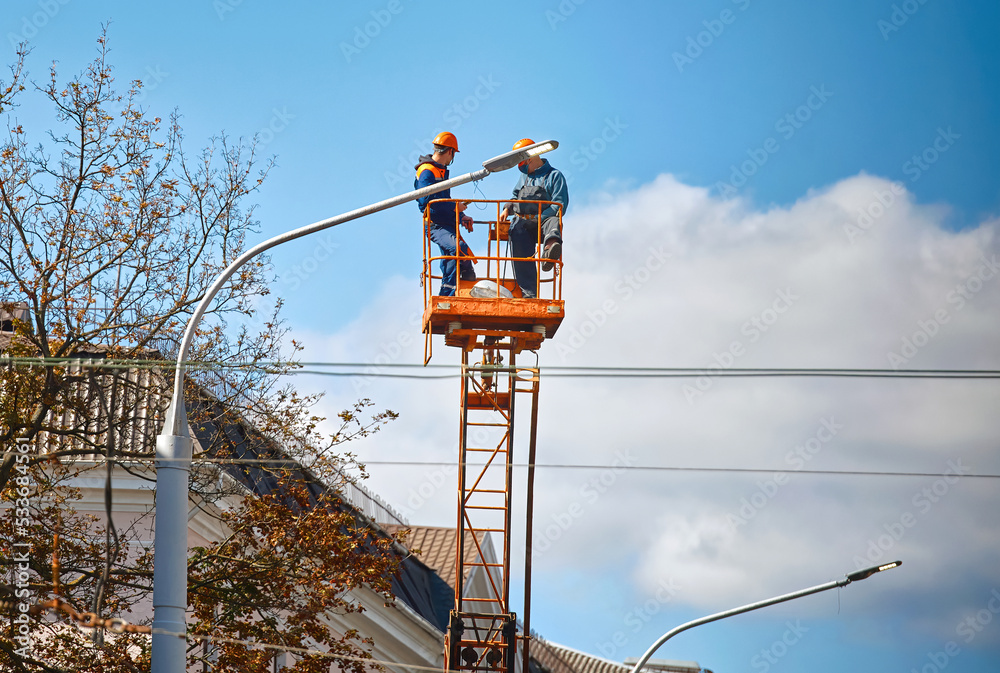 Workers on lifting platform installing new LED lamps. Electrician work ...