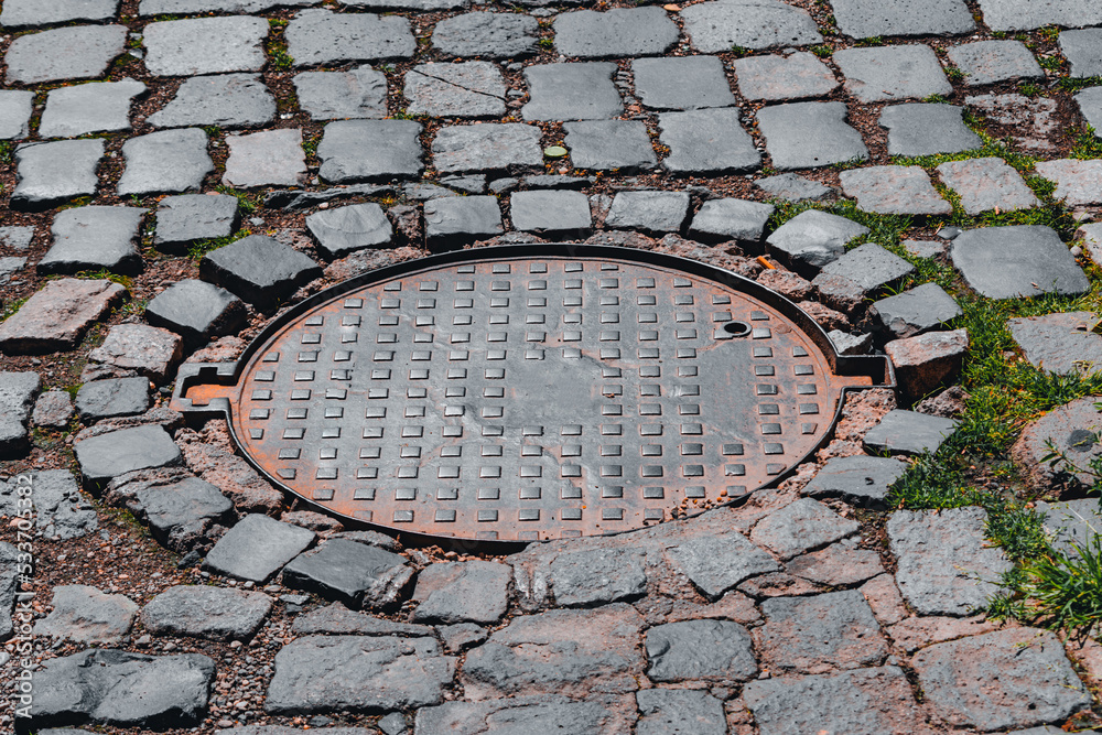 Round rusty metallic sewer cap or manhole cover on a paved road with ...