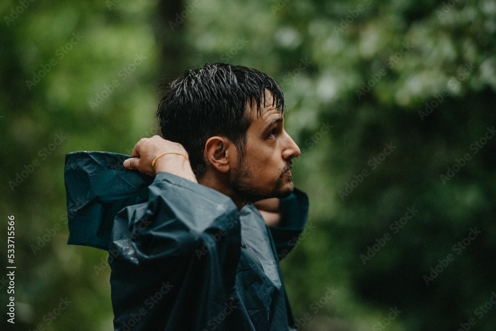 Man wearing a raincoat putting on his hood in the middle of a forest ...