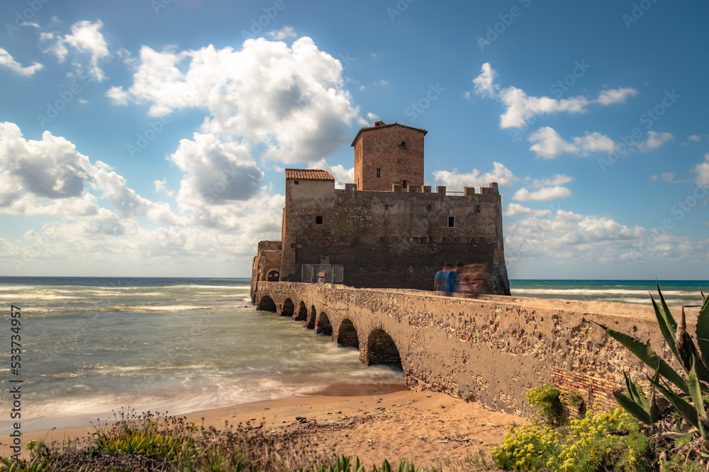 Foto de waves splash on the beach in front of the castle Torre Astura ...