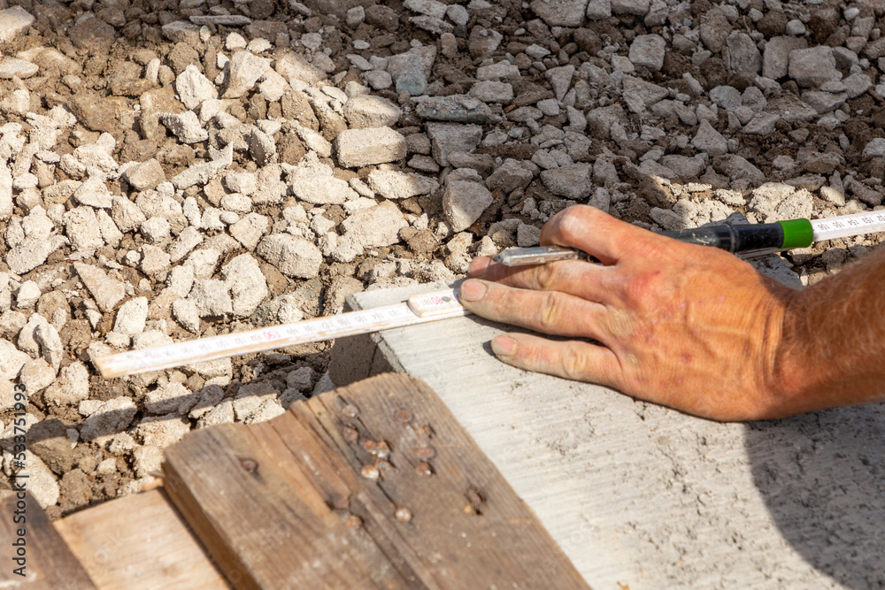 Drawing a straight line with a pencil on a concrete curb with ruler ...