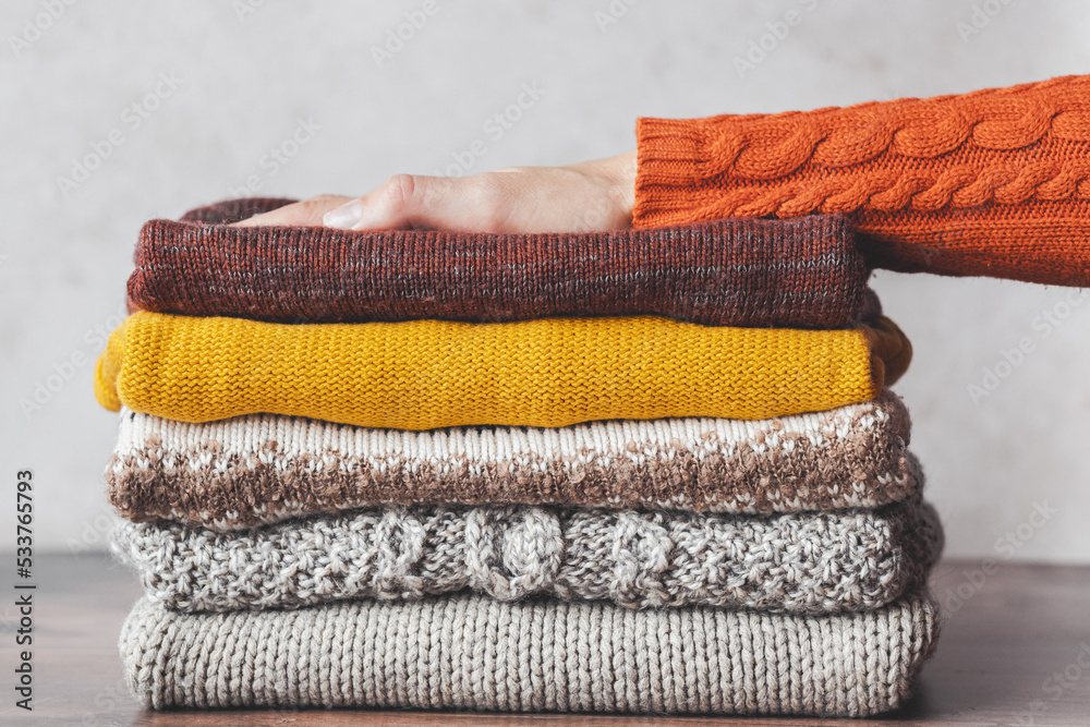 Bunch of knitted warm sweaters, females's hand on stack clothes of the ...