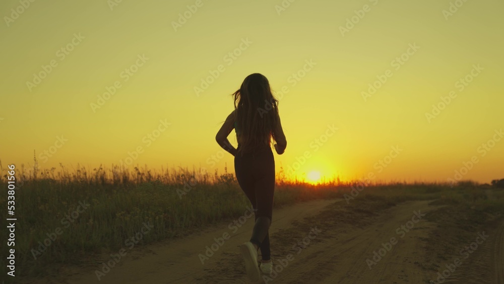 young girl runs across field sunset headphones. silhouette girl rays ...