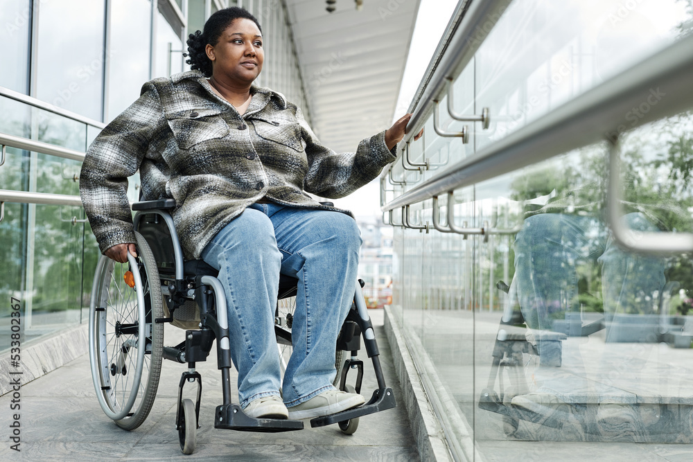Full length portrait of smiling black woman in wheelchair moving down ...